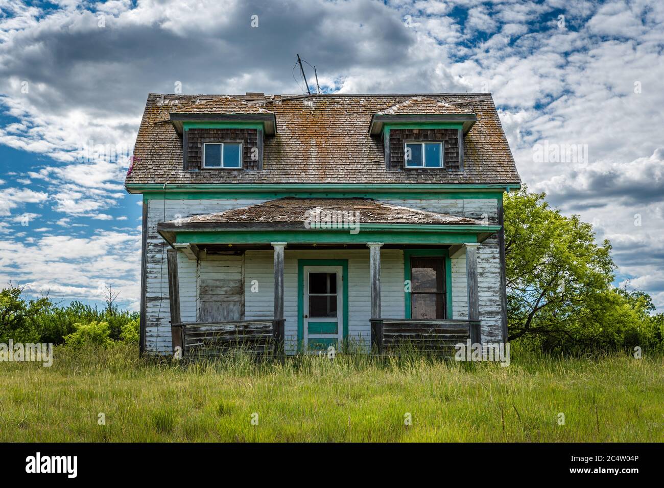 Old, abandoned prairie farmhouse with trees, grass and blue sky in ...