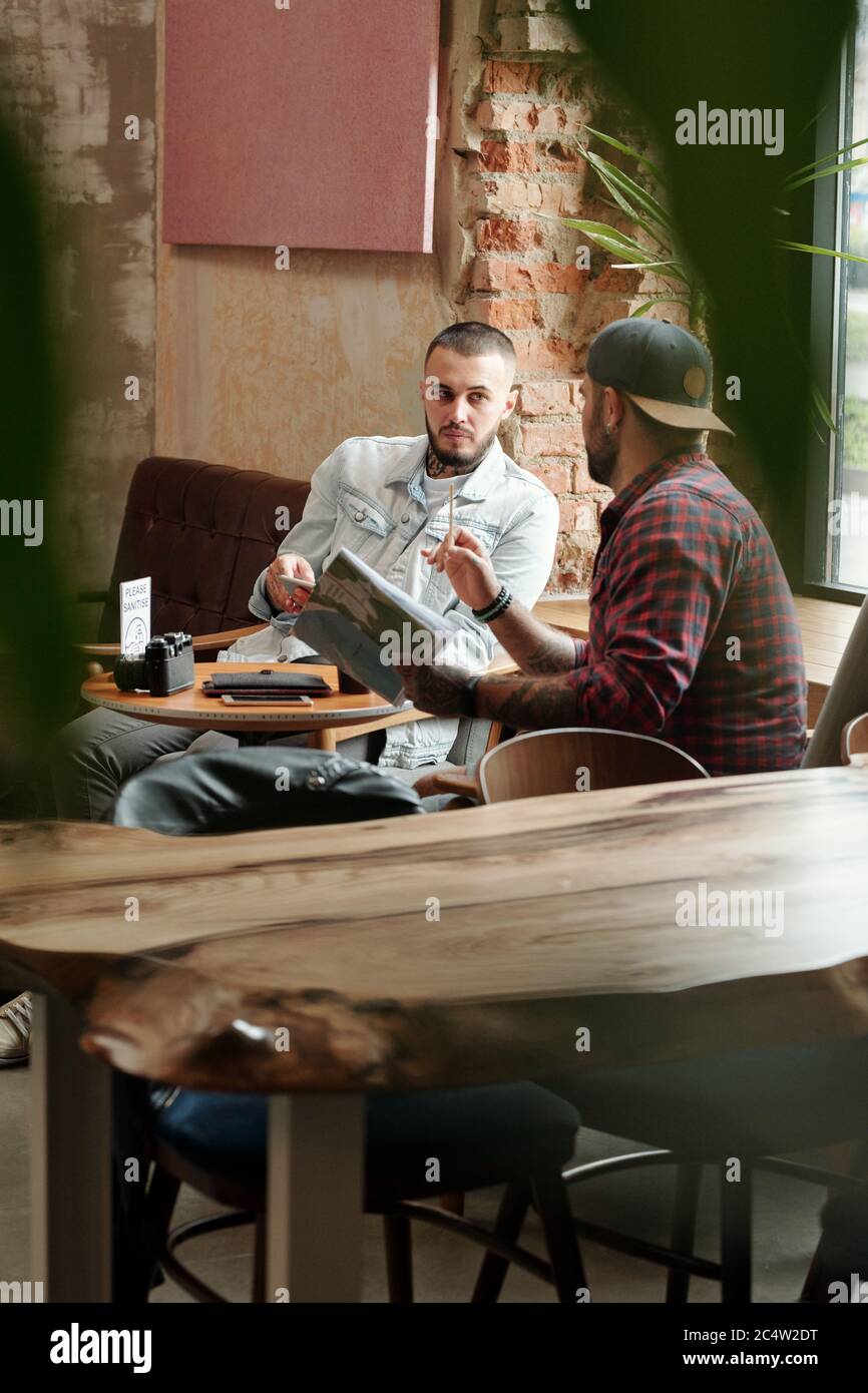 Modern young men sitting at table in empty cafe and brainstorming about ...