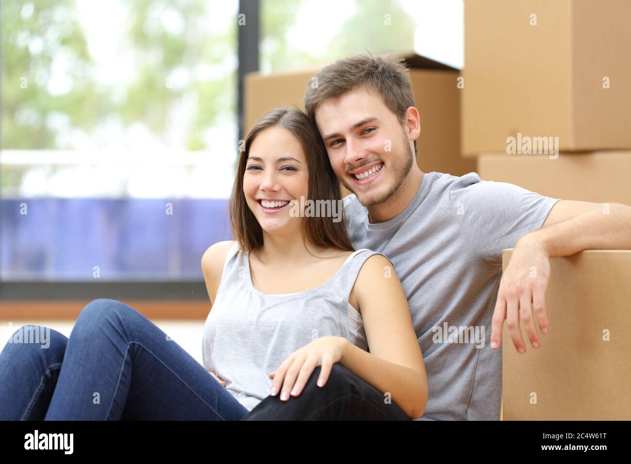 Happy couple moving looking at camera at new home in the living room ...