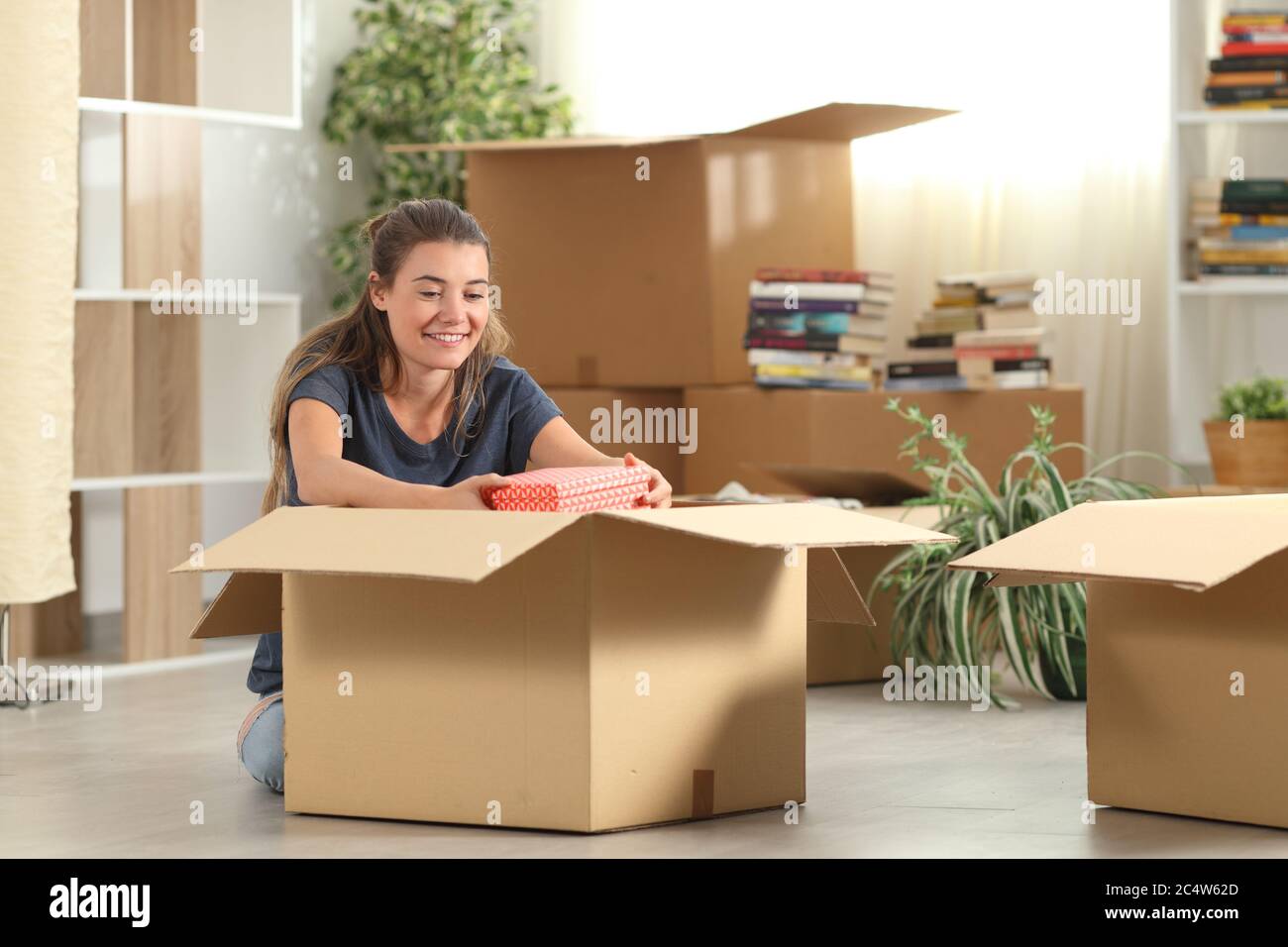 Happy girl unpacking boxes moving to new home sitting on the floor in ...
