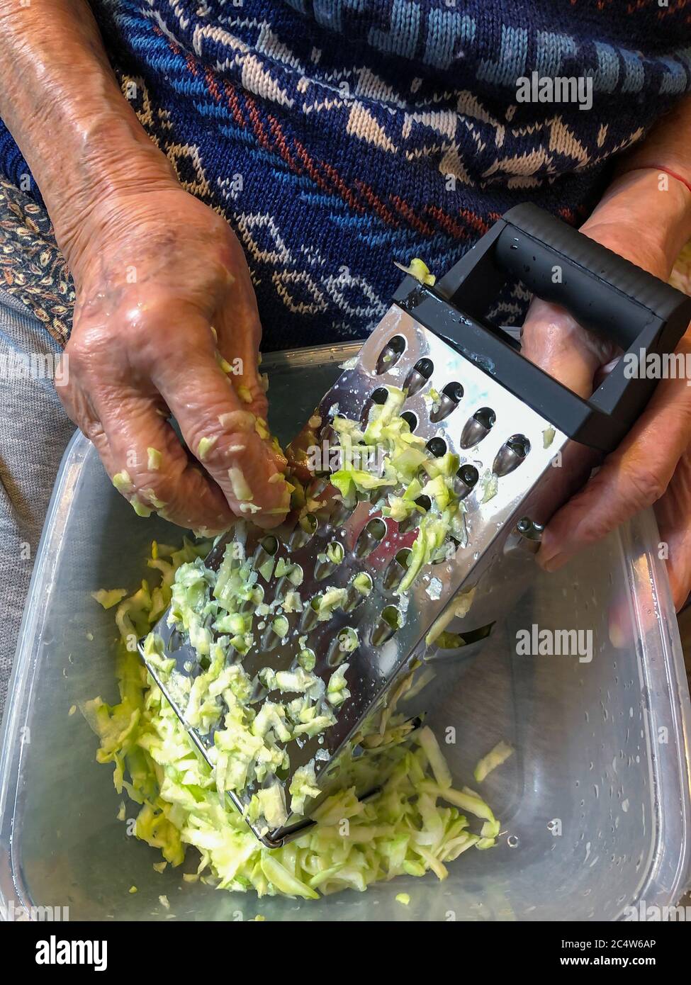 closeup wrinkled hand of a senior person grating zucchini in to a bowl ...