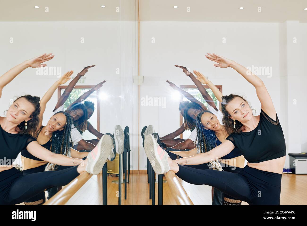 Pretty smiling young dancers putting feet on barre when doing ...