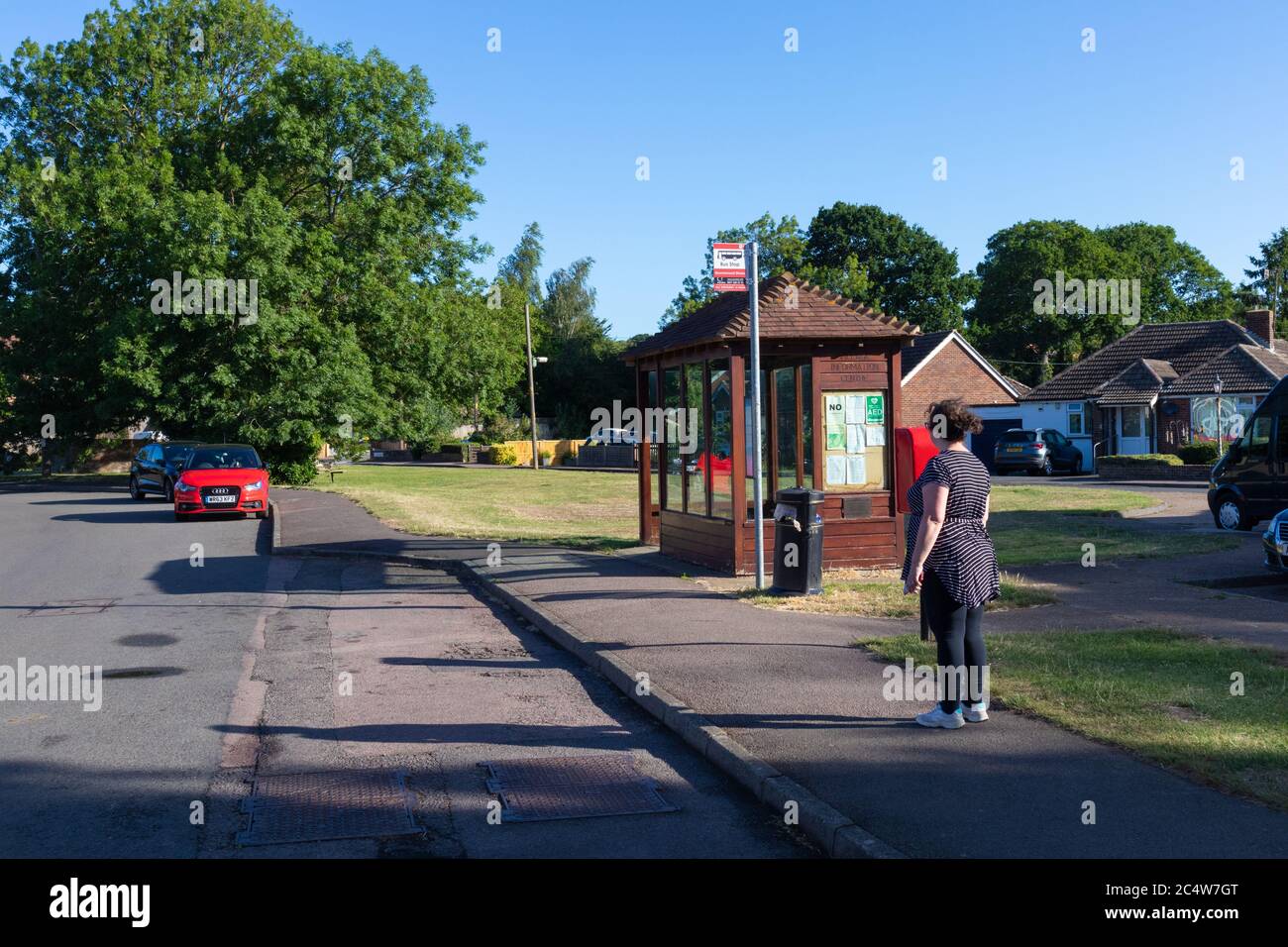 Woman waiting for bus at rural bus stop, hamstreet village, kent, uk ...