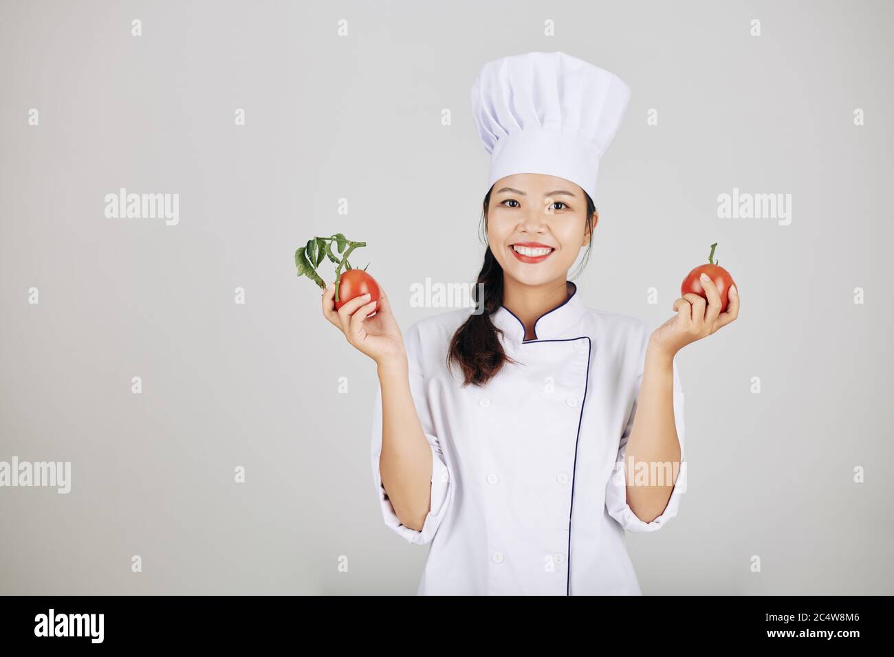 Pretty smiling restaurant chef showing fresh ripe tomatoes she used for ...