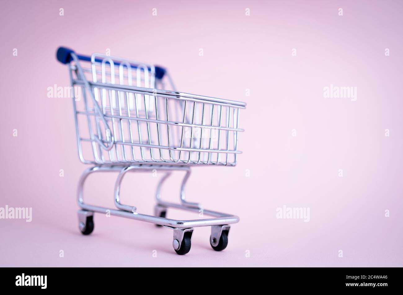 empty shopping cart over light pink background, mini metal cart ...