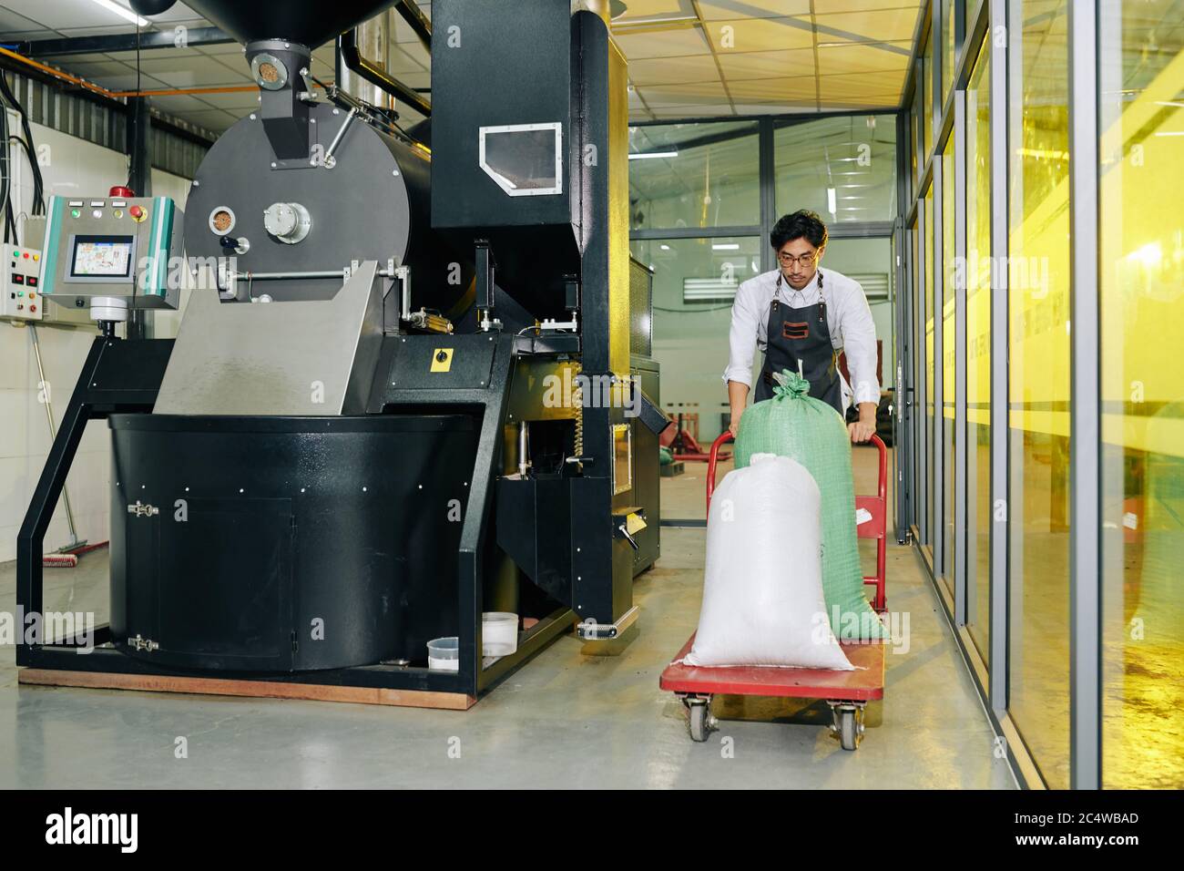 Barista pushing cart with sacks of coffee beans he roasted at roastery ...