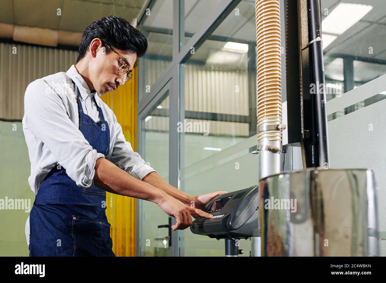 Serious small business owner pushing button on coffee roaster machine ...