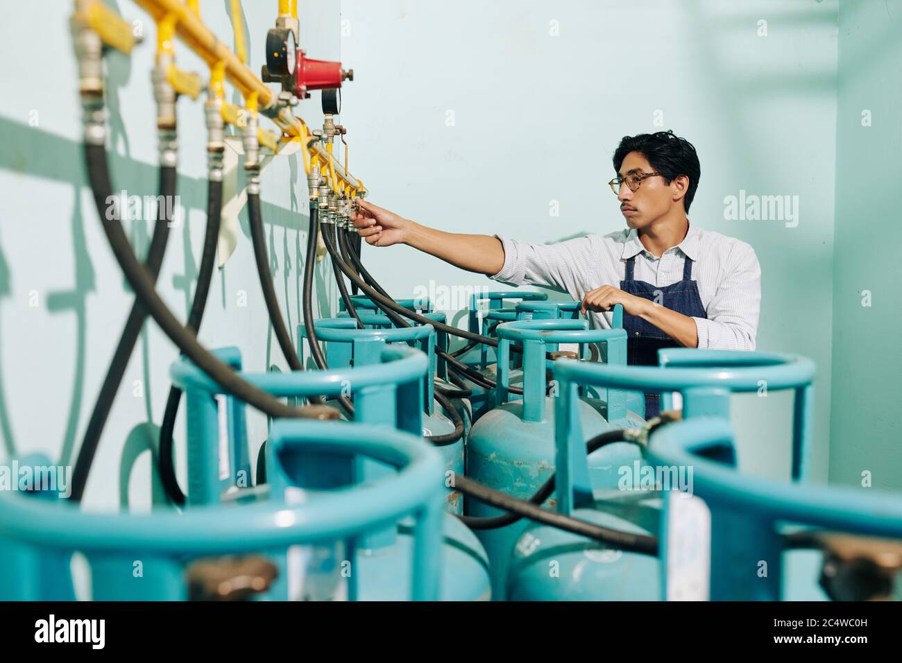 Mixed-race coffee roastery worker attaching rubber hoses to gas pipe ...