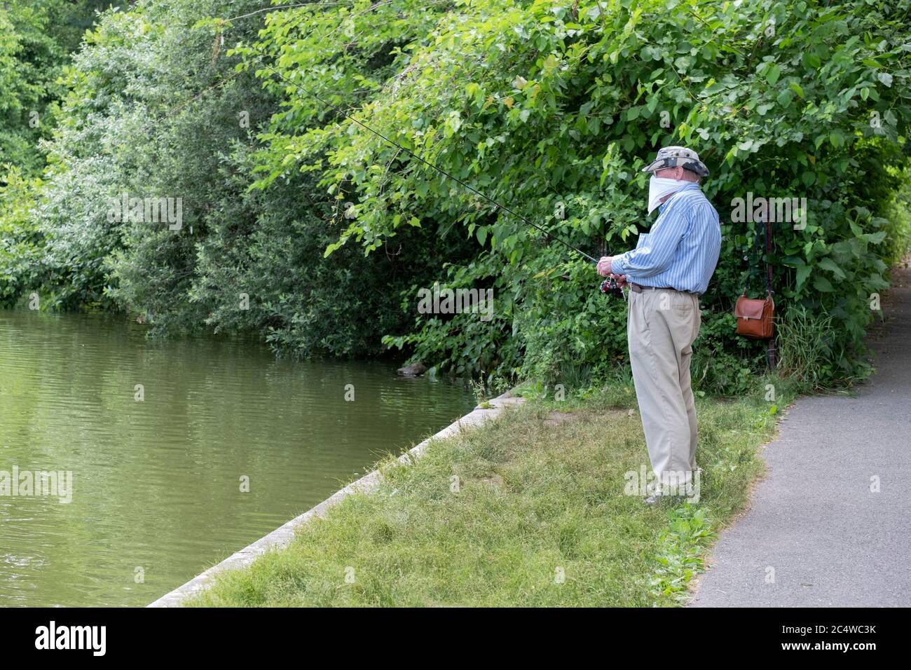 An older man wearing a bandana fishes in Kissena Lake in Kissena Park ...