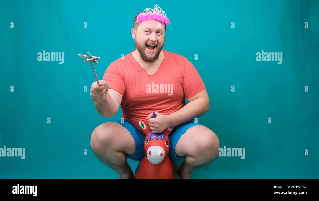 cute bearded freaky man in a pink T-shirt with a diadem on his head ...