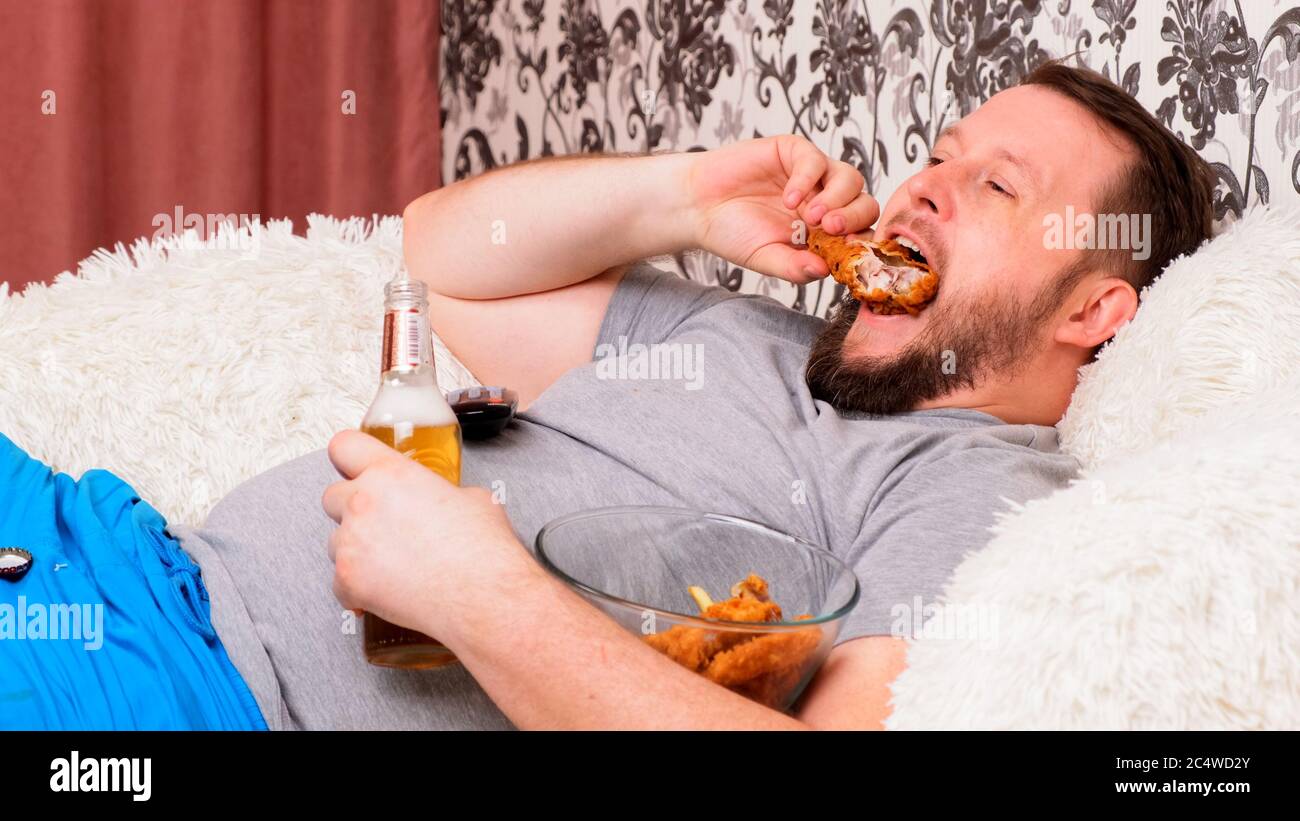 fat man drinks beer and eats unhealthy food chicken wings, bored in ...