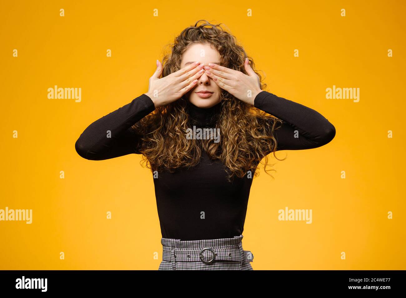 Pretty girl hide her face with hands isolated on yellow background ...