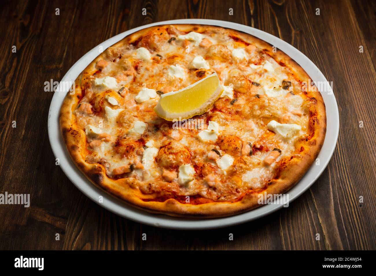 Fish and feta cheese pizza with a slice of lemon, wooden background ...