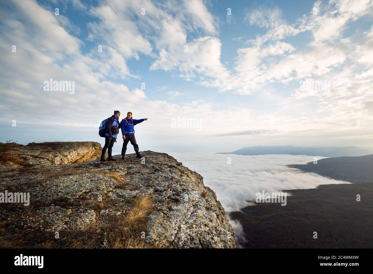 Two climbers standing on top of summit above clouds in the mountains ...