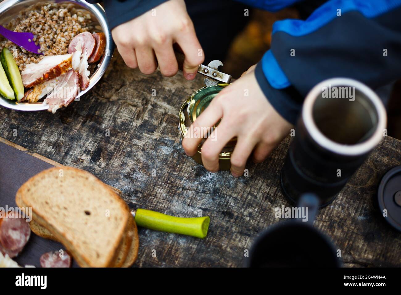 Hiker opens cans on wooden table during breakfast at the forest camp ...