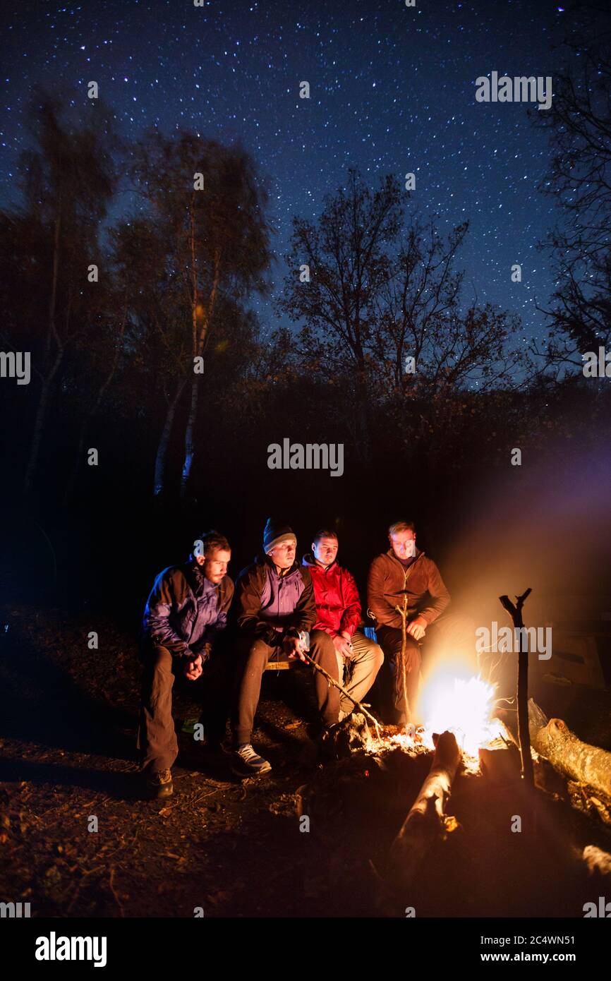 Long exposure photo of four hikers sitting around bonfire and warming ...