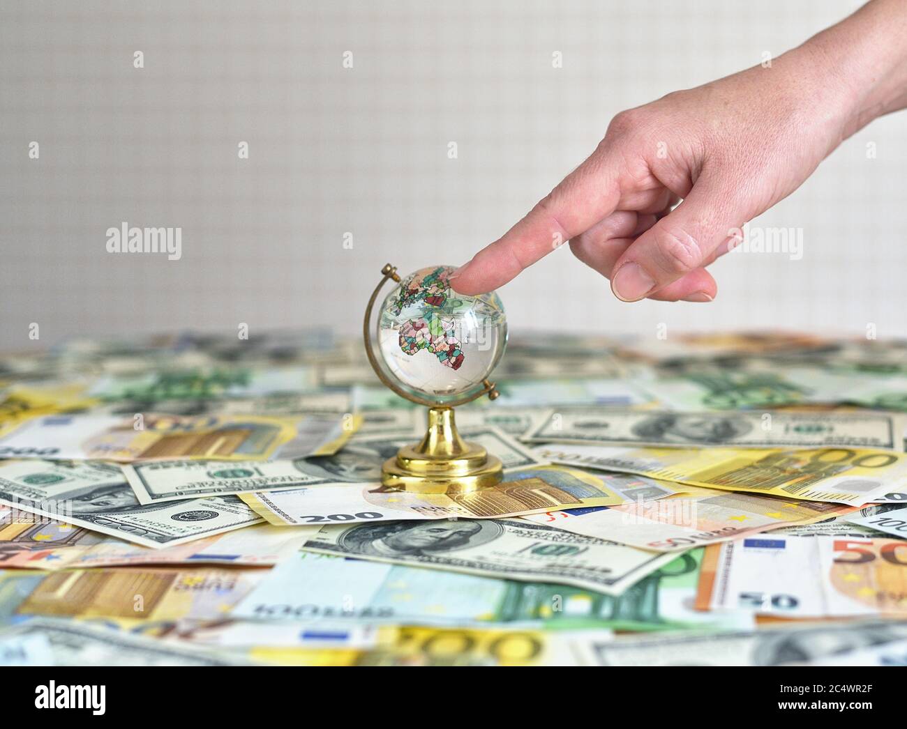 little globe on the table with money. female hand indicates a place on ...