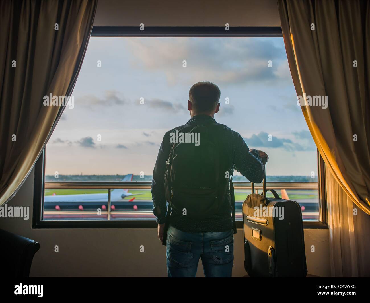 A young man watches the airplane take off from the window of his hotel ...