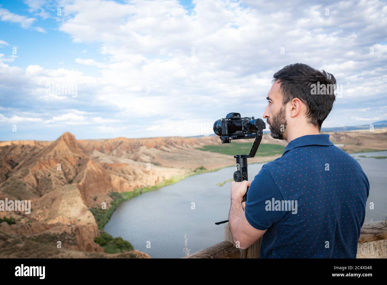 young filmmaker filming natural landscape in canyon with a large river ...