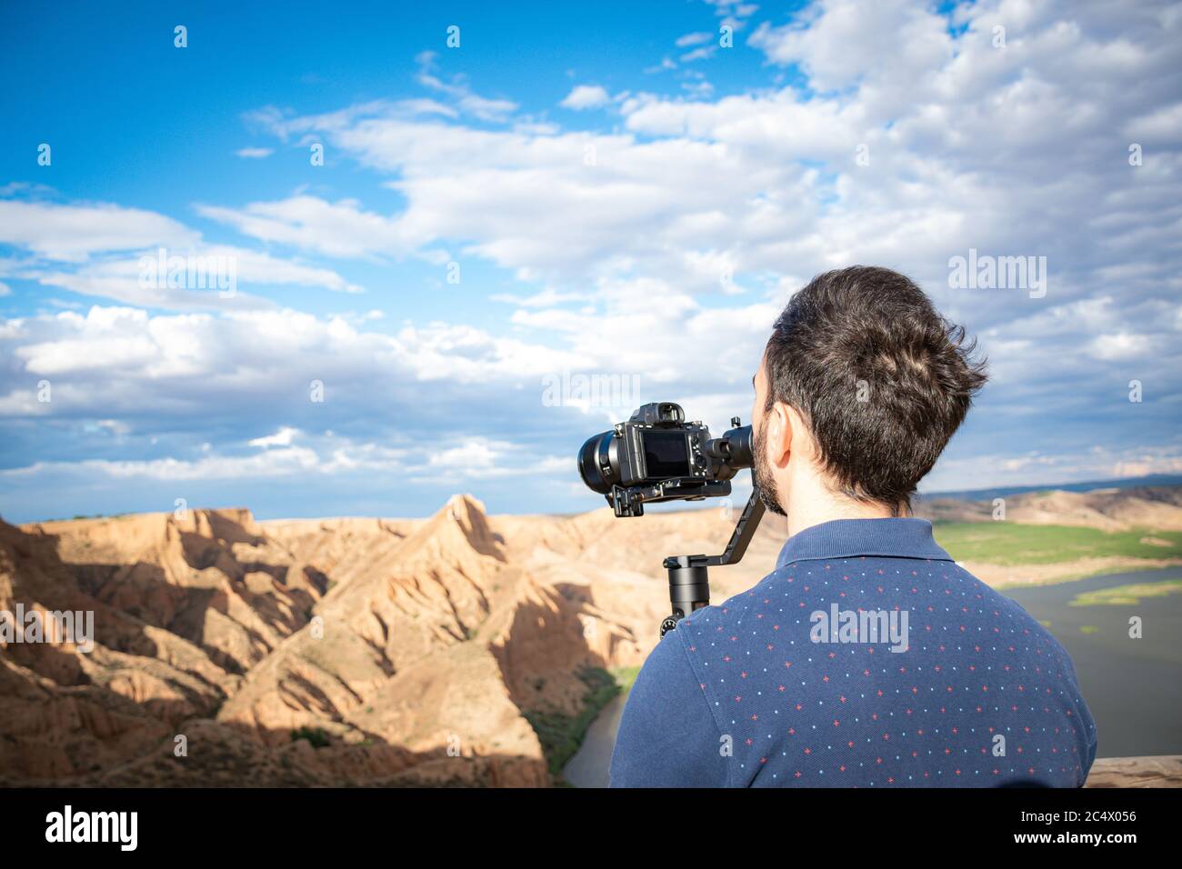 young filmmaker filming natural landscape in canyon with a large river ...