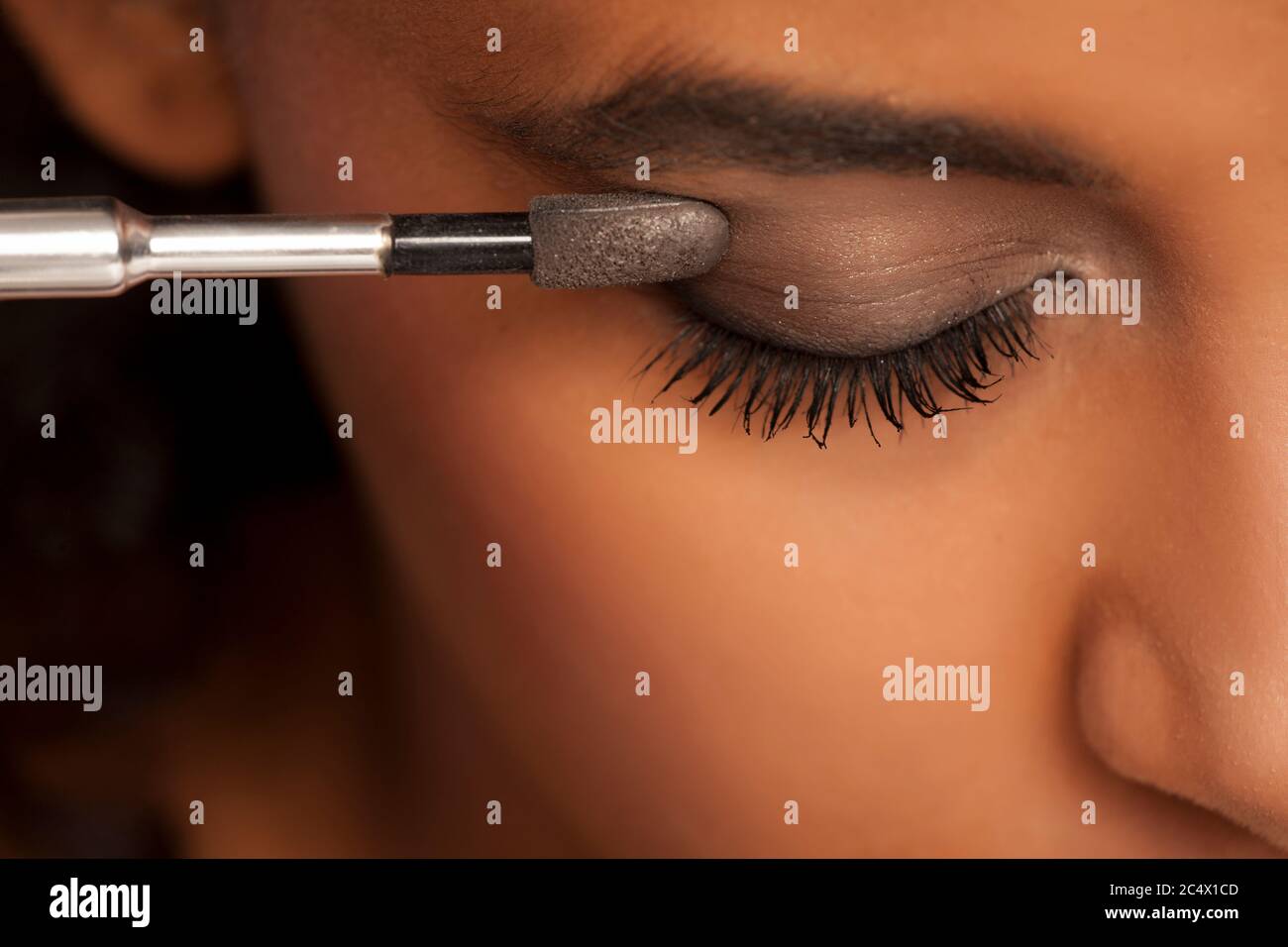 portrait of a young dark-skinned woman applying eye shadow with ...