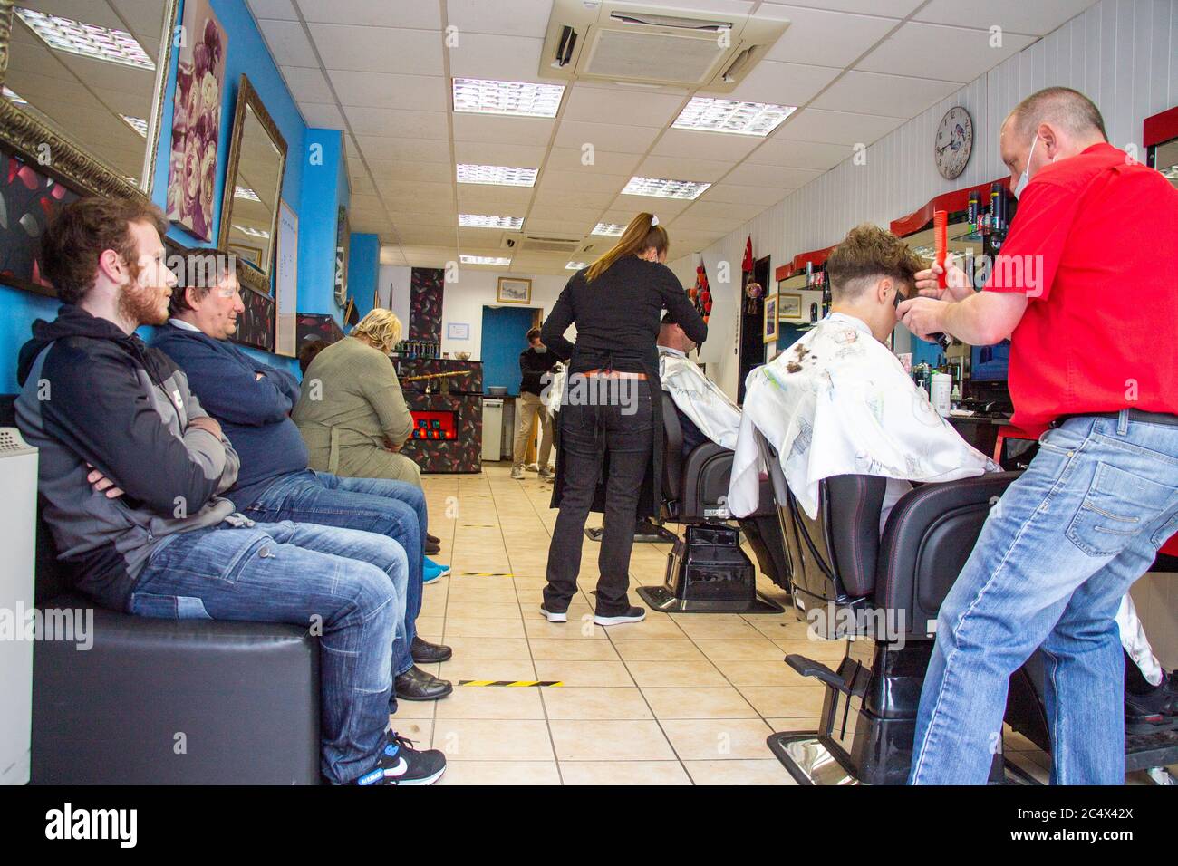Male Barber wearing a face mask cutting a mans hair in a barbers shop ...