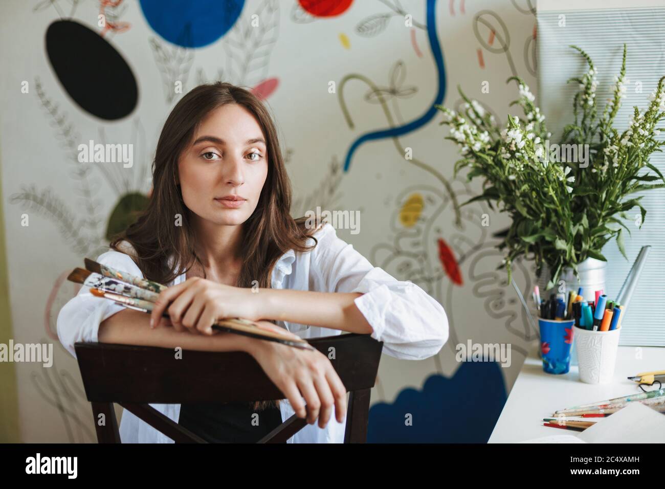 Beautiful painter in white shirt on chair dreamily looking in camera ...