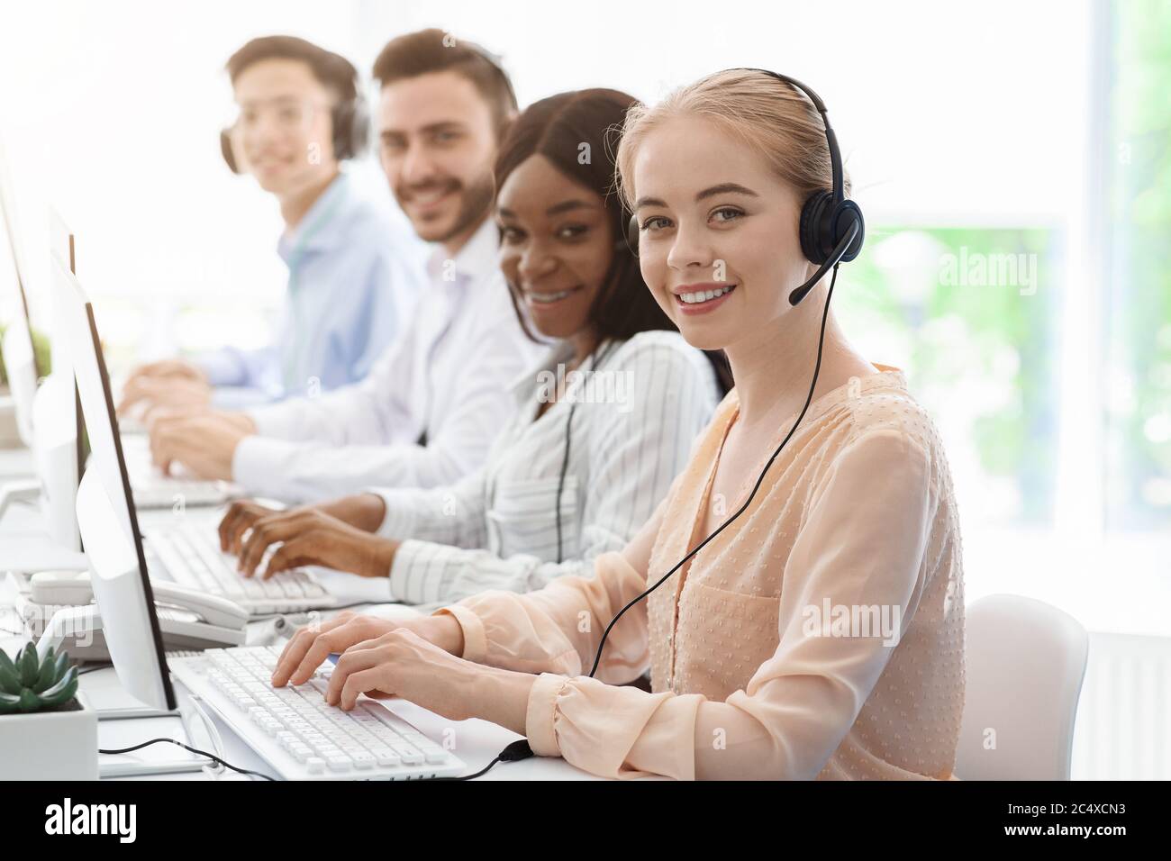 Group of call centre employees smiling and working on computers at ...