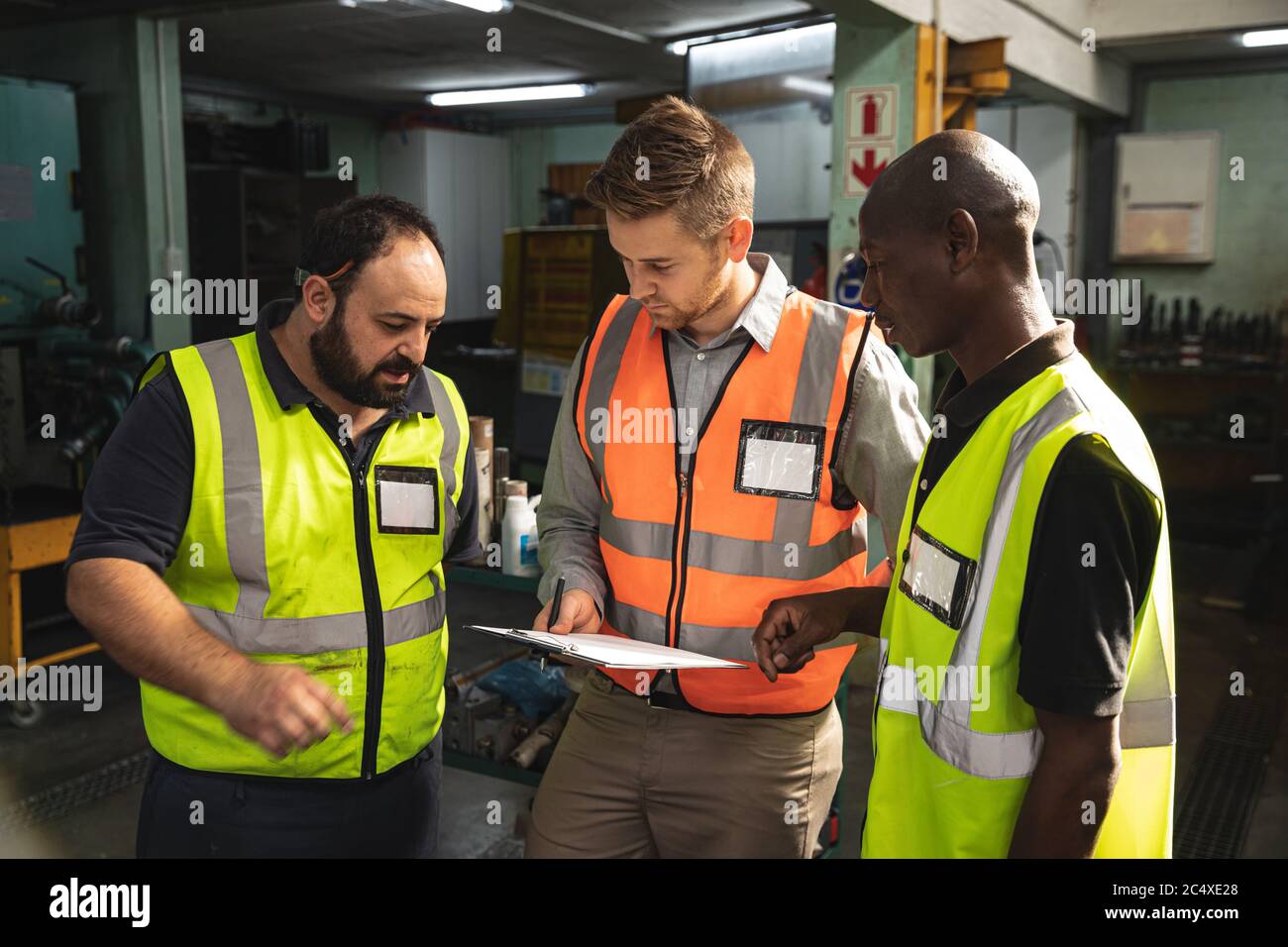 Three male factory workers discussing over a clipboard at the factory ...