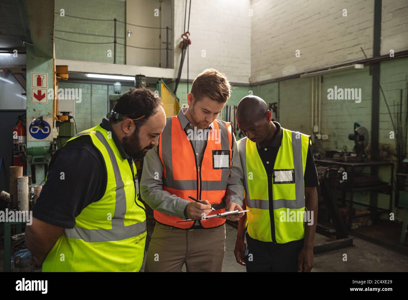 Three male factory workers discussing over a clipboard at the factory ...
