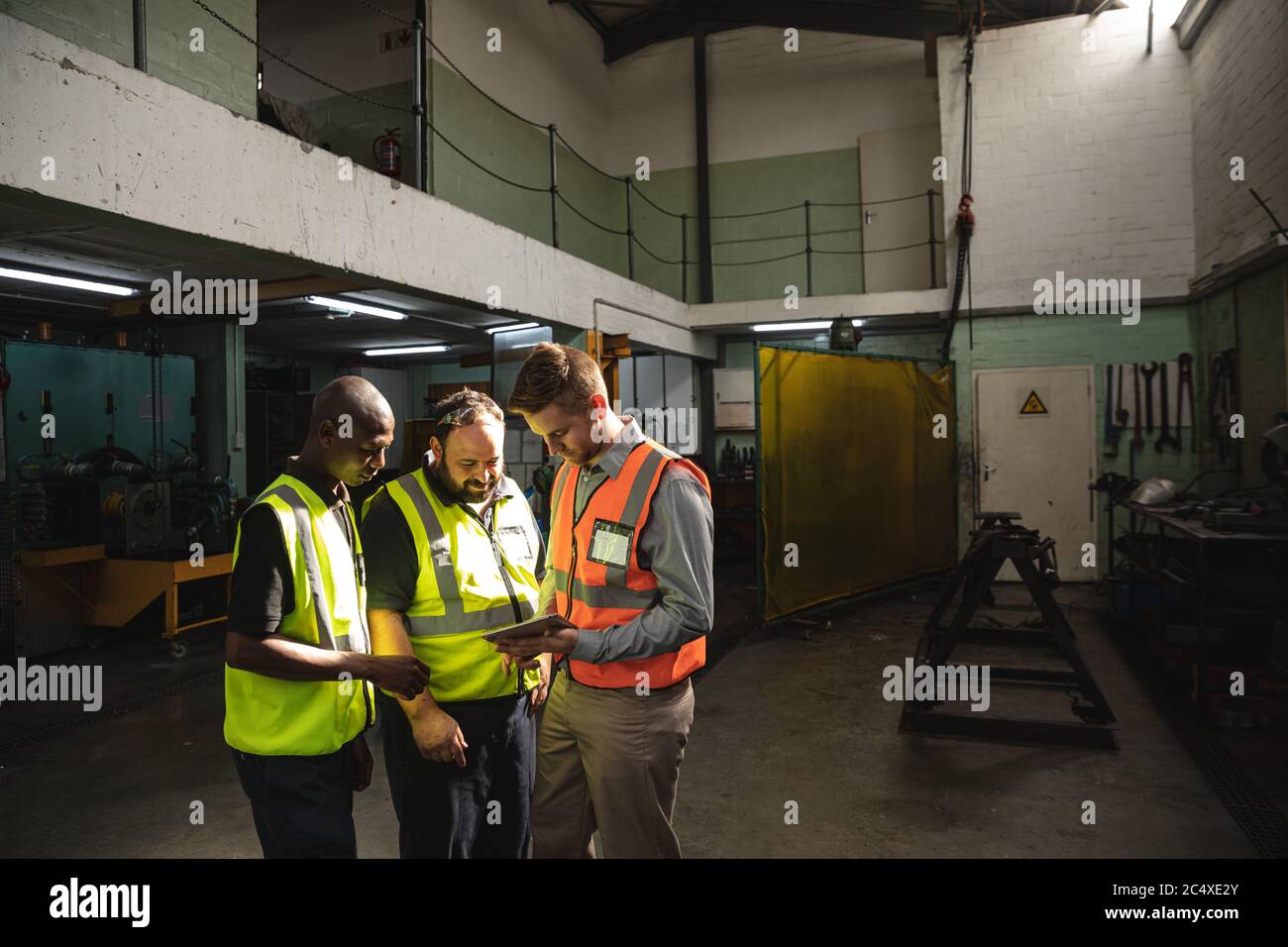 Three male factory workers discussing over a digital tablet at the ...