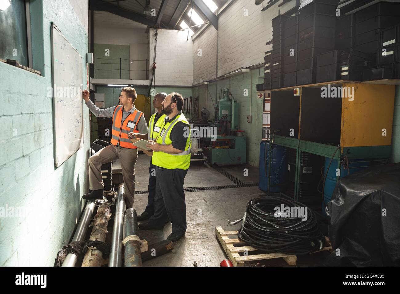 Three male factory workers discussing over a whiteboard at the factory ...