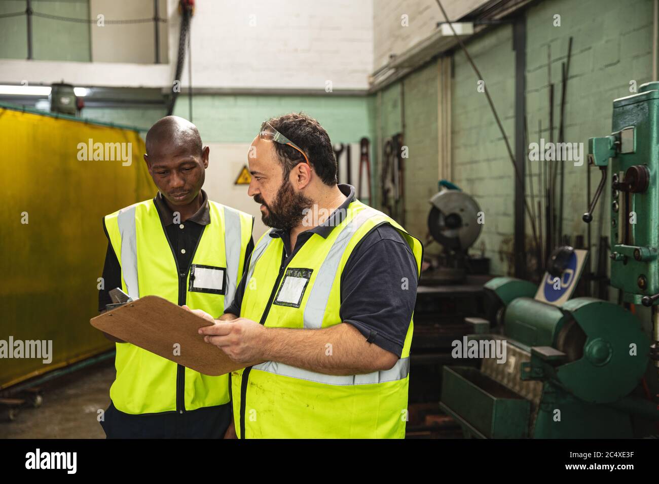Two male factory workers discussing over a clipboard at the factory ...