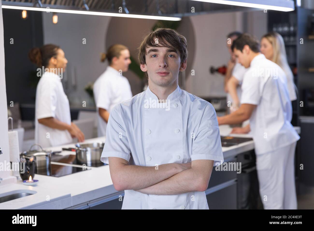 Portrait of young male chef standing with his arms crossed at ...