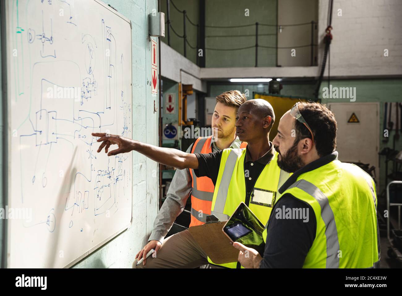 Three male factory workers discussing over a whiteboard at the factory ...
