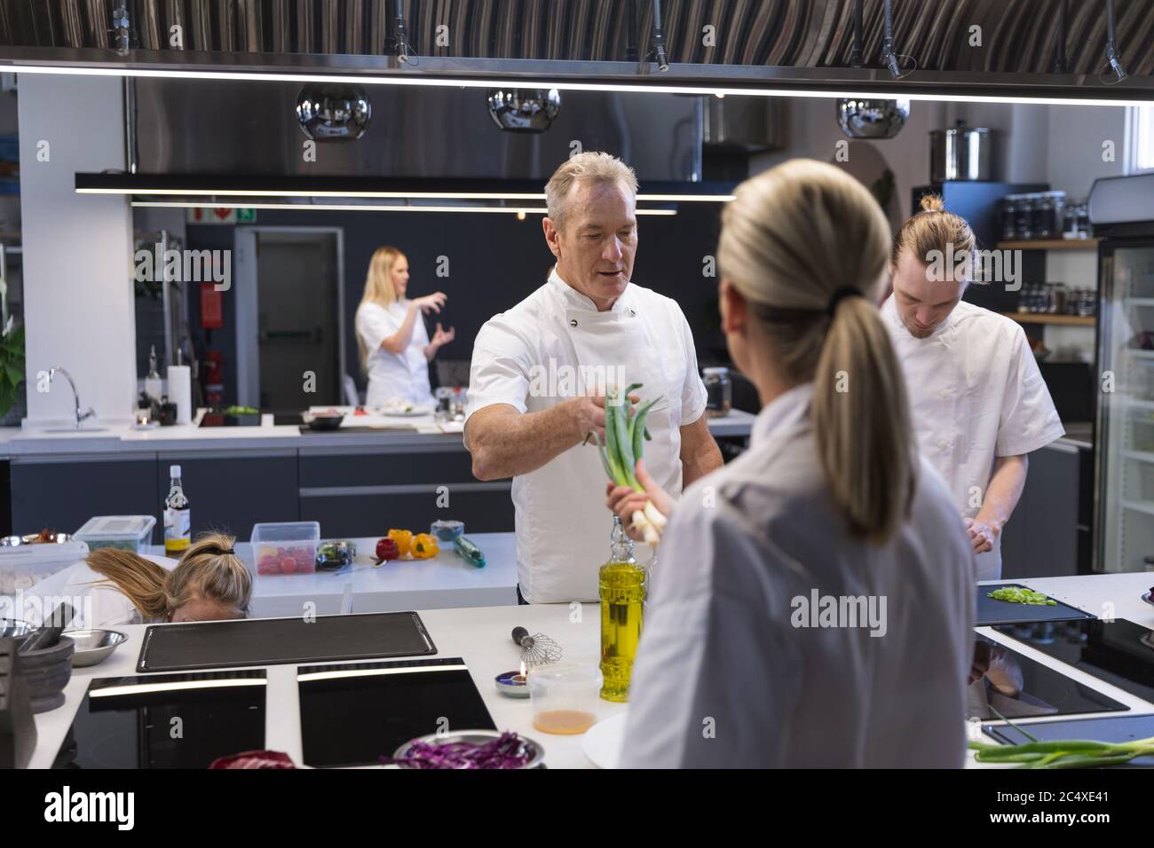 Female chef passing leek vegetable to male senior chef at restaurant ...