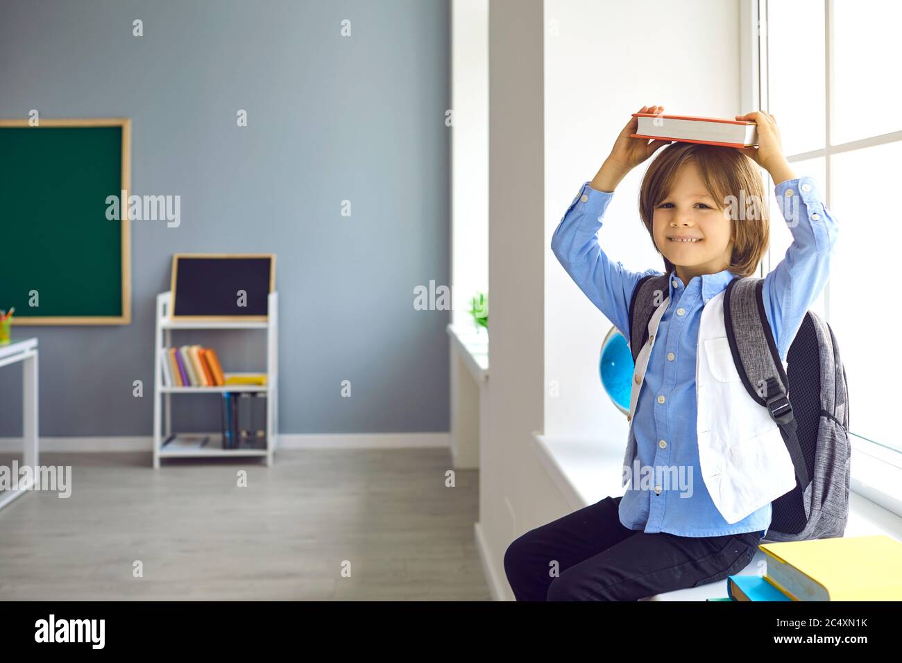 Cute schoolboy holds a book over his head in a school class. First time ...