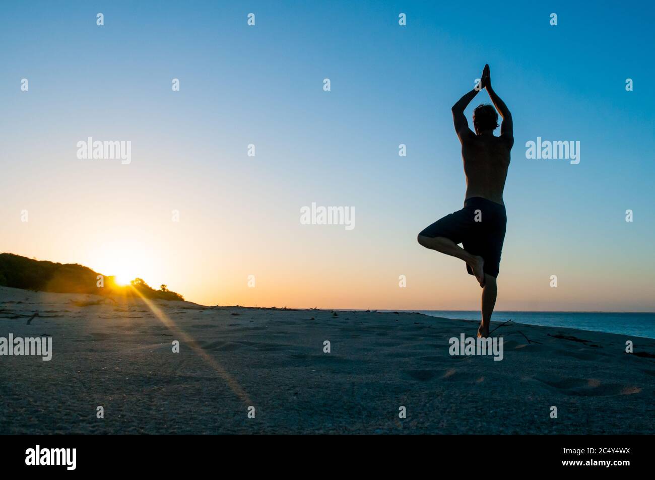 Fit young man practices sun salutation yoga on the beach at sunset ...