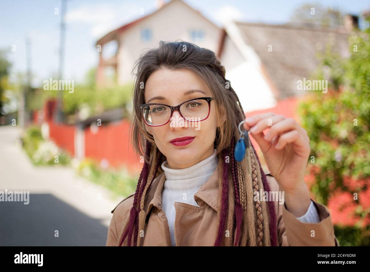 Modern young girl with long dreadlocks and eyeglasses is showing bunch ...