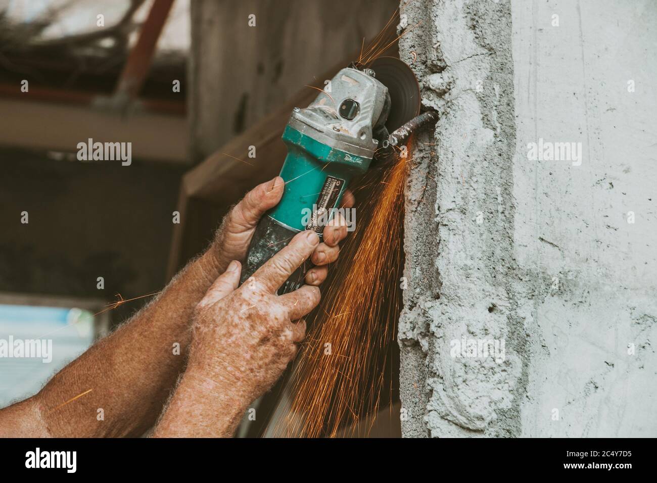 An elder man's hands grip an electric cut off tool igniting sparks ...