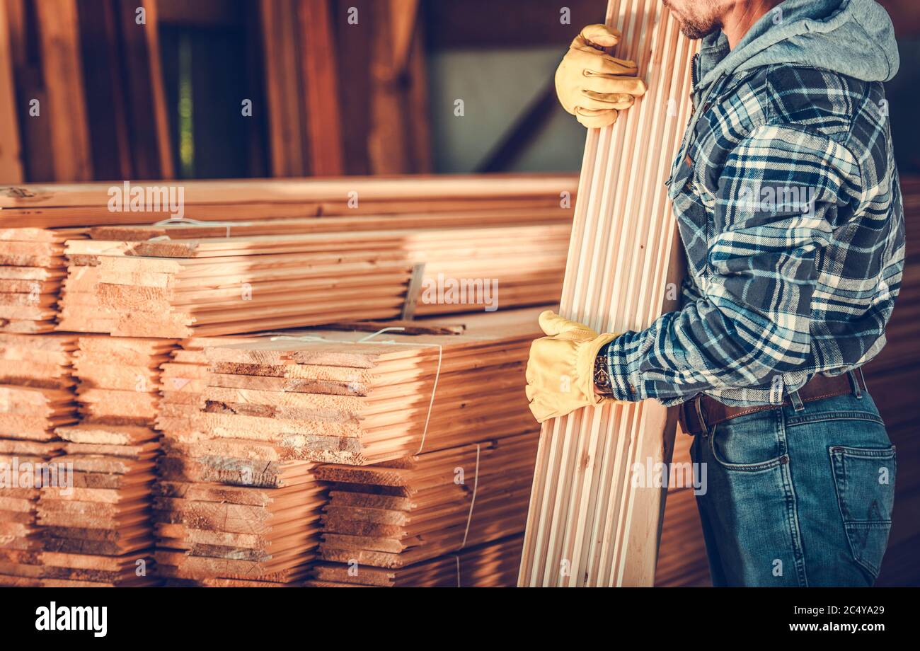 Male Worker Picking Up Bundle Of Lumber From Stack Of Wooden Planks At ...