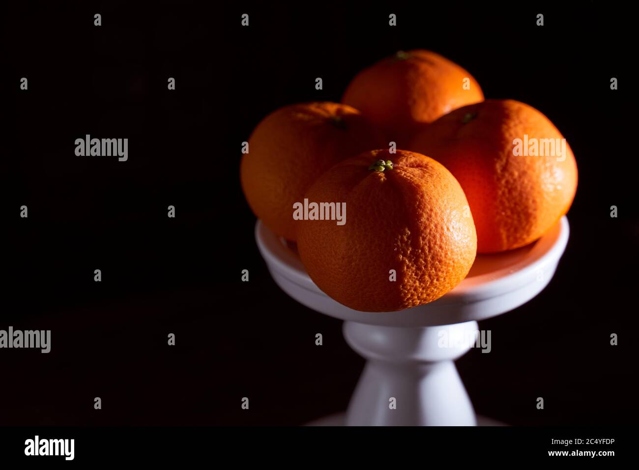 Four tangerines lie on a white stand. Black background. Concept photo ...