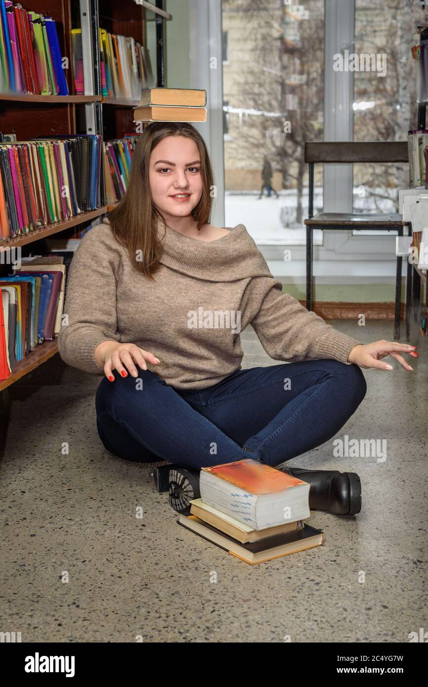 Brunette Young Girl Sitting On The Floor And Balancing Stack Of Books