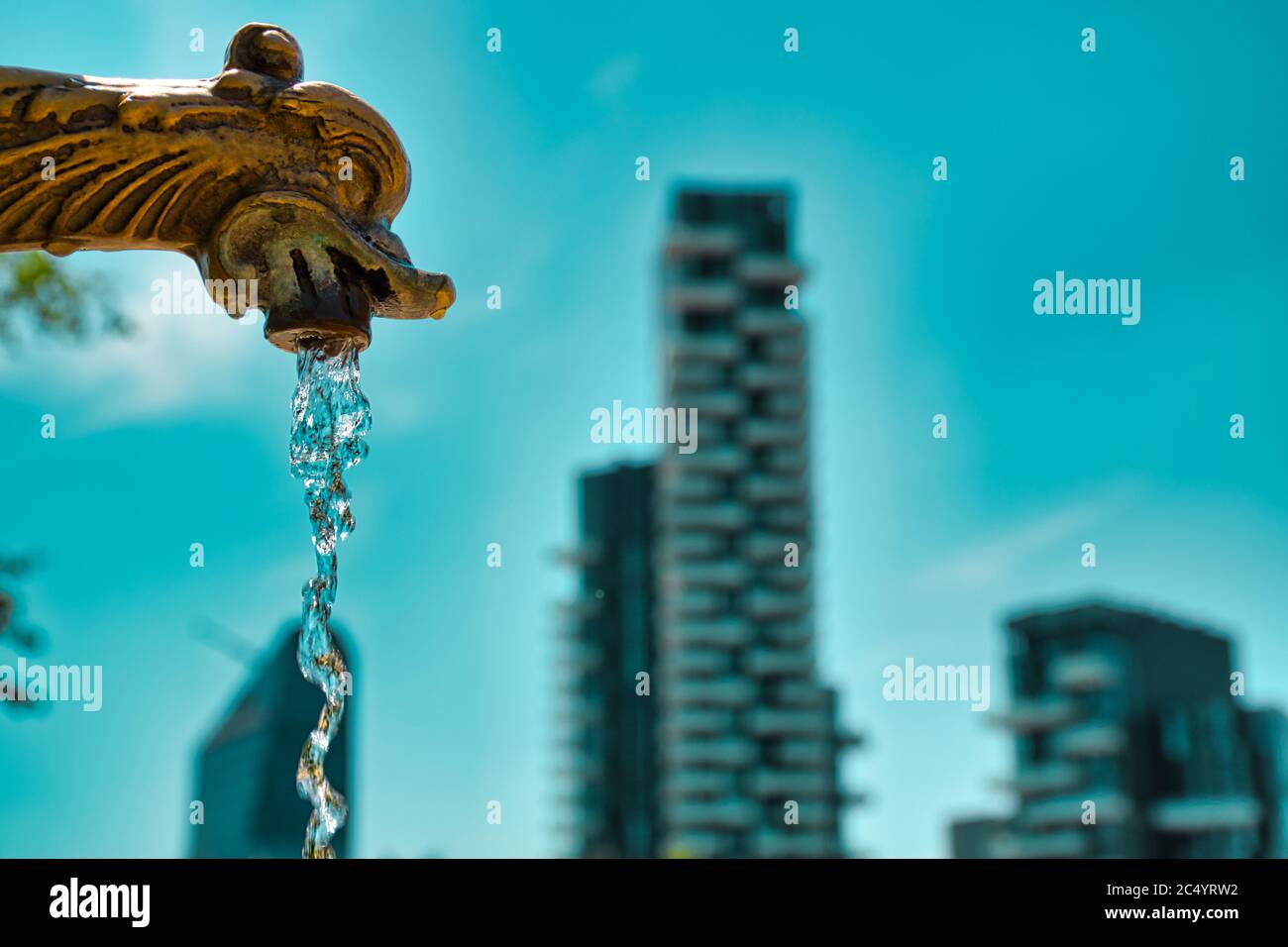 Closeup view of water flows from a well with skyscrapers in the ...