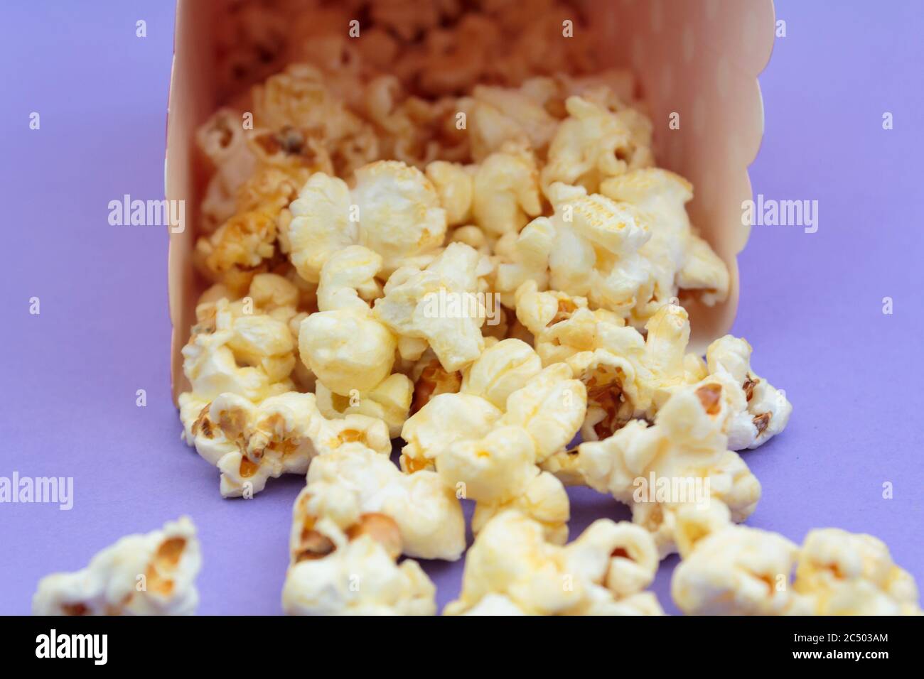 Popcorn falling out of the box on purple background Stock Photo - Alamy