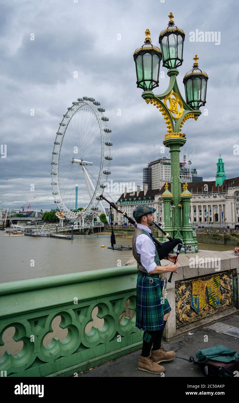 A bagpipe player dressed in Scottish highland clothing busking on ...