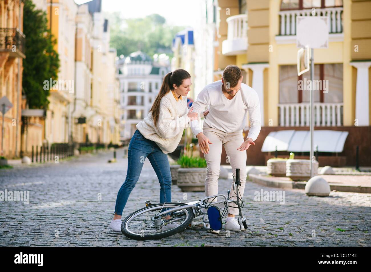 Woman helping man near bike on road Stock Photo - Alamy
