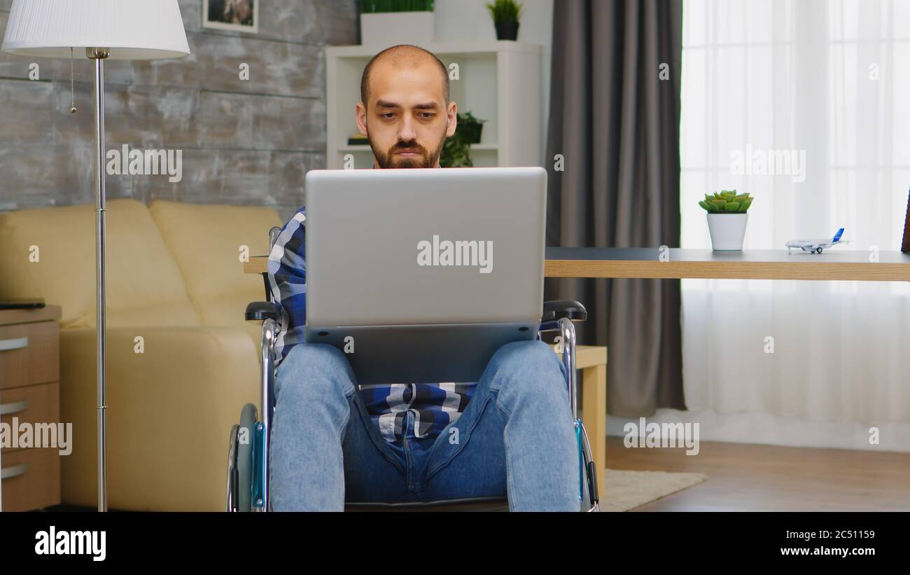 Invalid man in wheelchair working on laptop from home Stock Photo - Alamy