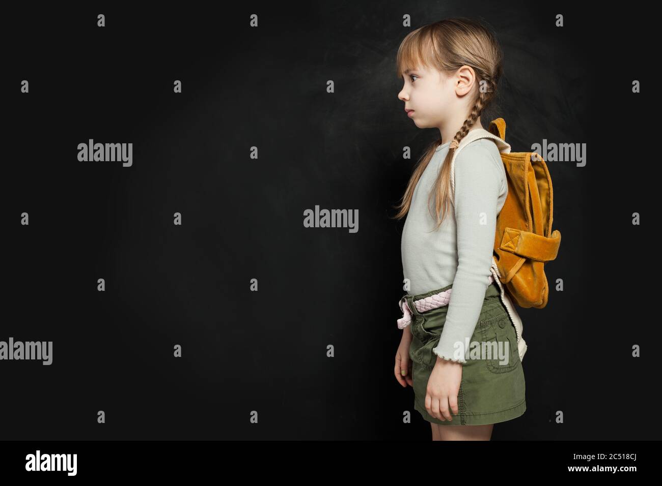Sad school child girl standing with backpack on black. School problem ...