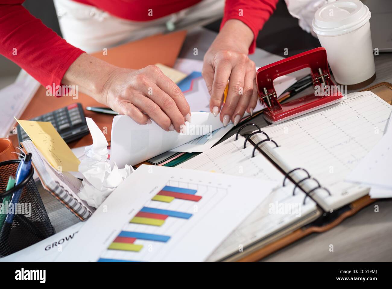 Disorganized businesswoman looking for documents on her messy desk ...